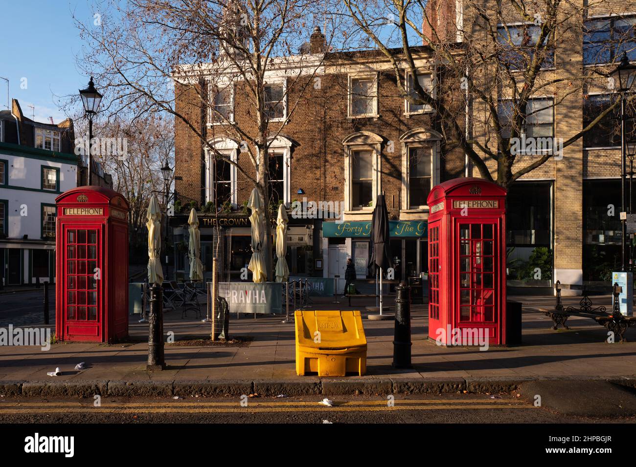 Early morning sun falls on a yellow salt bin and two traditional red ...