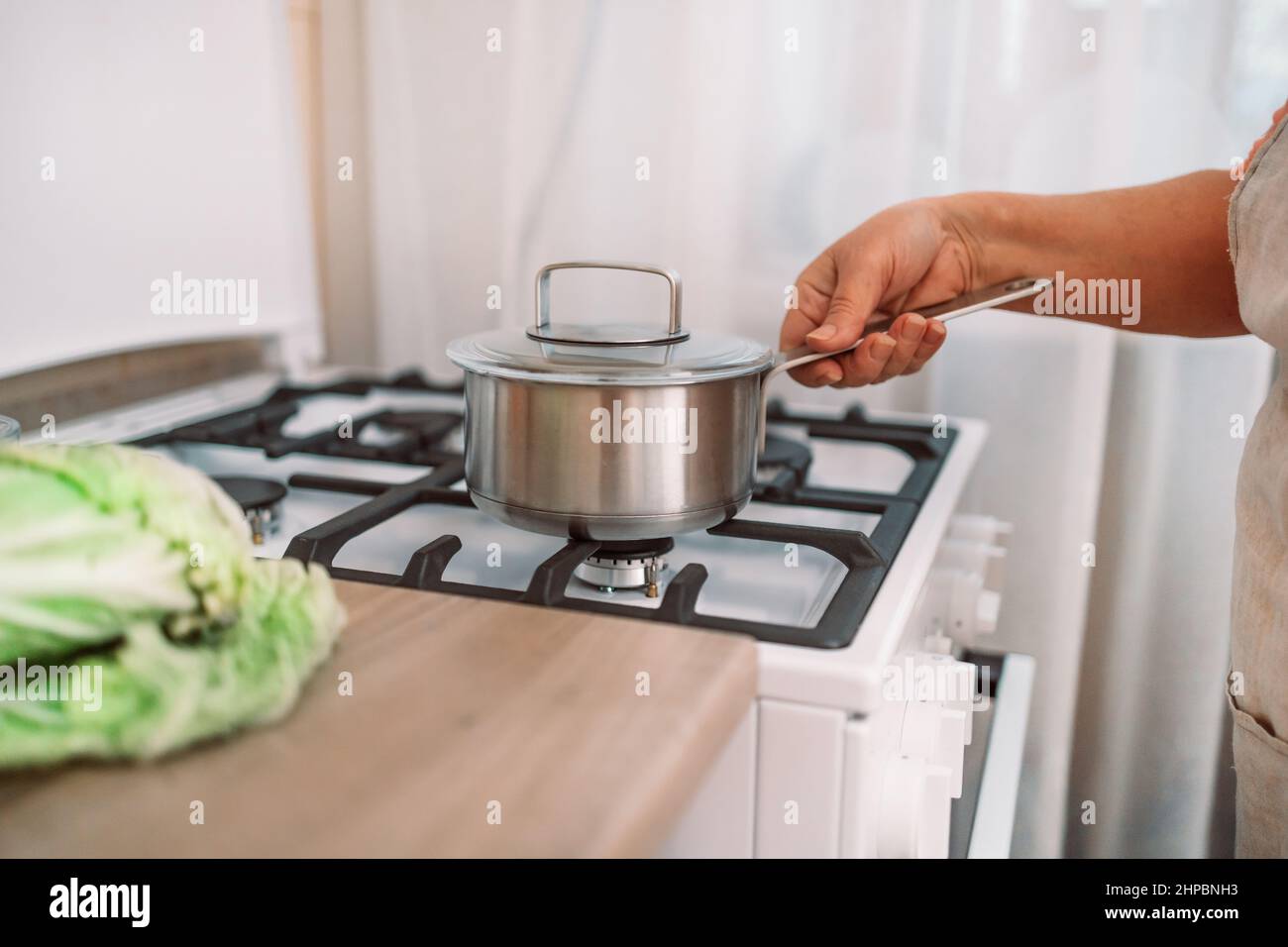 Woman puts stainless steel pot on gas stove in modern kitchen. Cooking ...