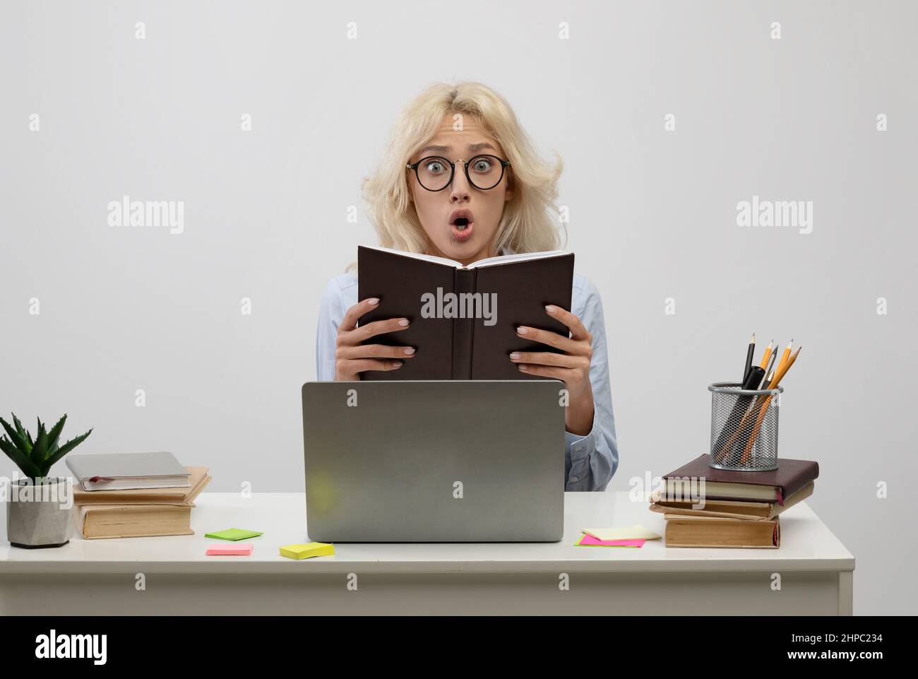 Shocked female secretary holding notepad and looking at camera in shock ...