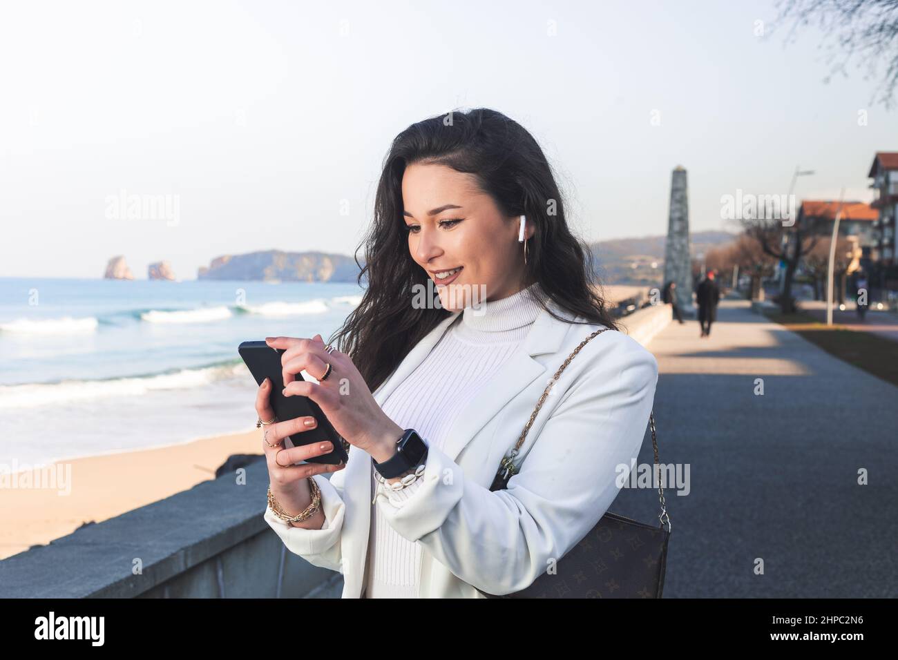 Young caucasian woman using a smartphone at the sea promenade of ...