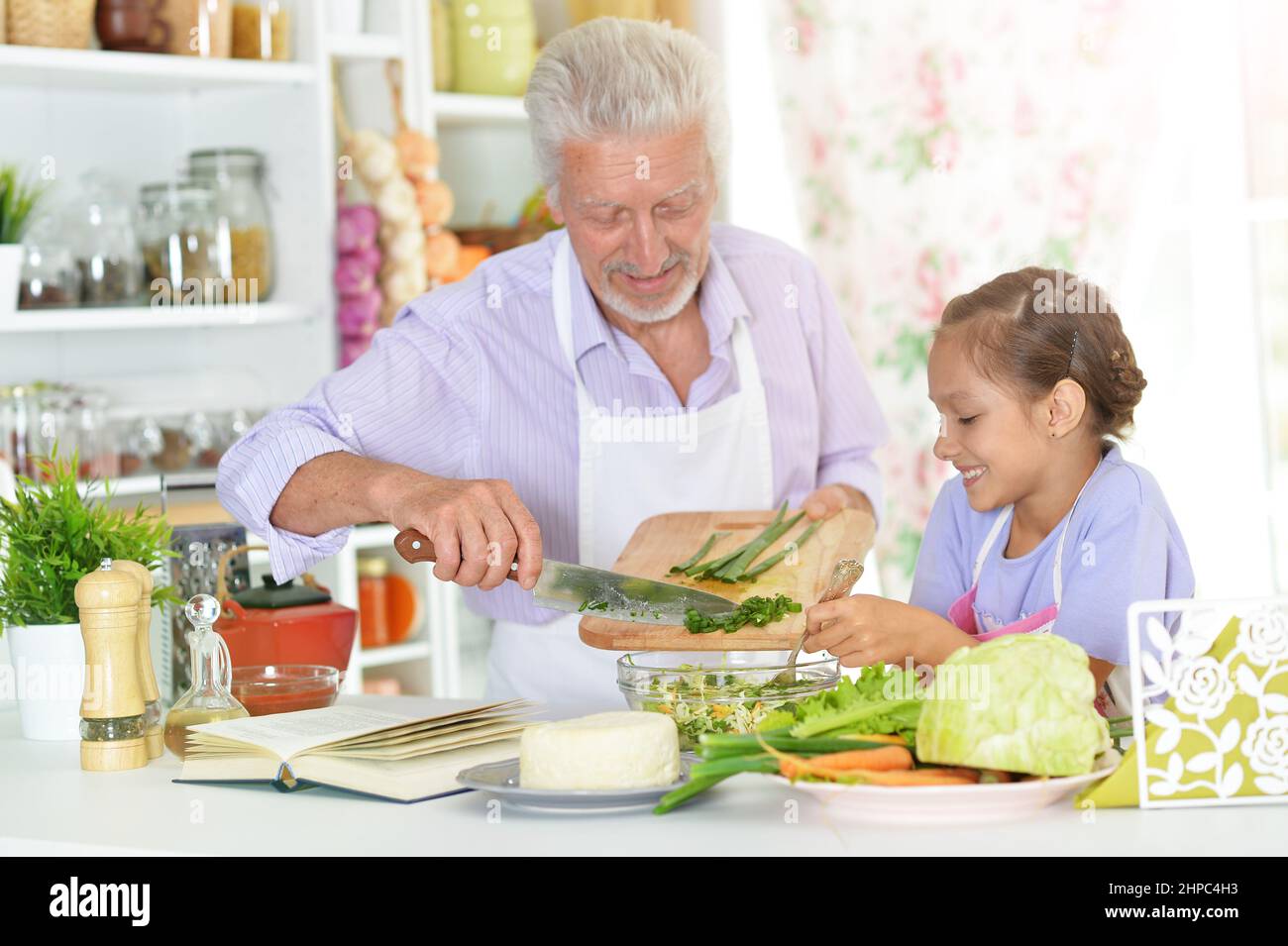 Senior man in chefs uniform preparing dinner with his granddaughter ...