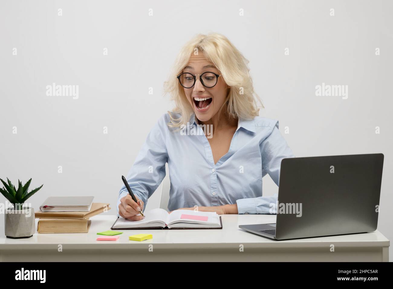 Surprised businesswoman working on laptop and taking notes in notebook ...