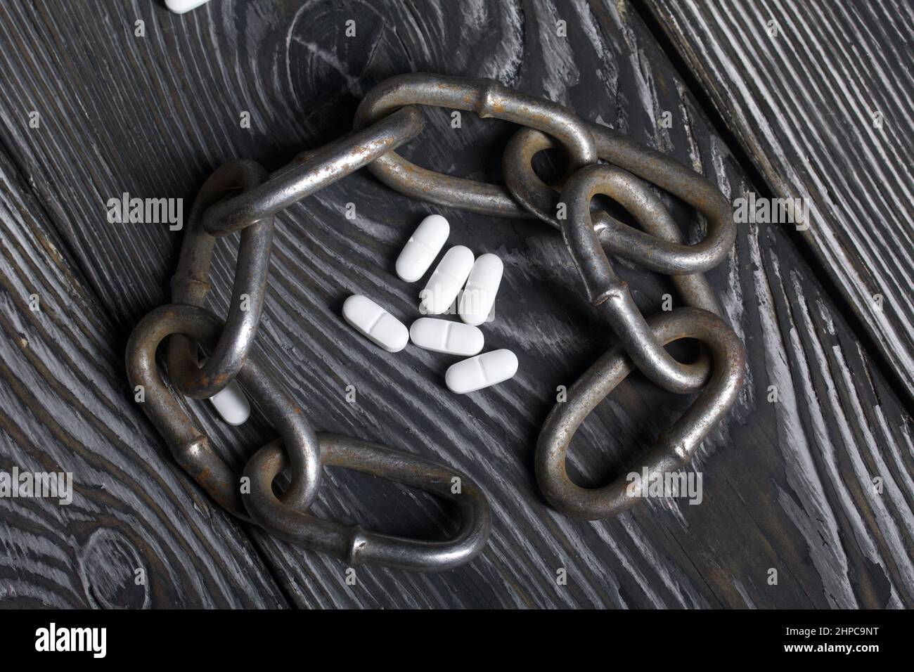 White tablets. Metal chain. Symbol of drug addiction. On black pine ...