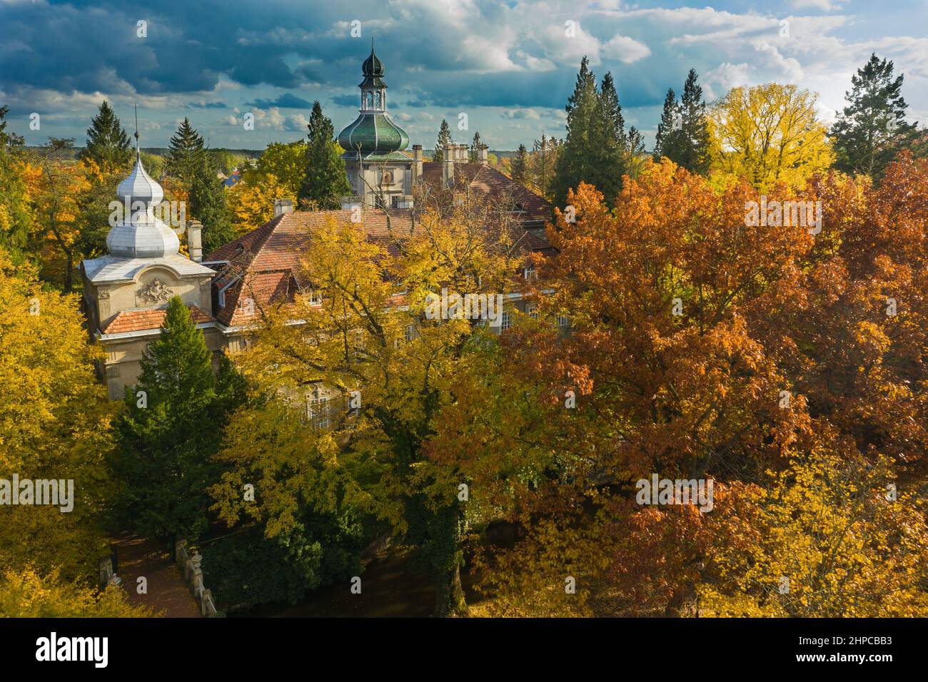 A palace situated among tall trees. It is fall, the leaves on the trees ...