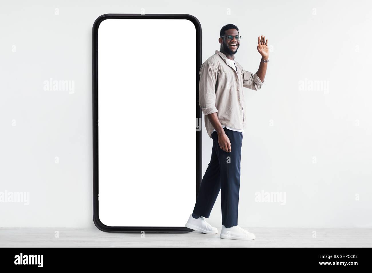 Happy black guy standing next to giant smartphone with white screen and ...