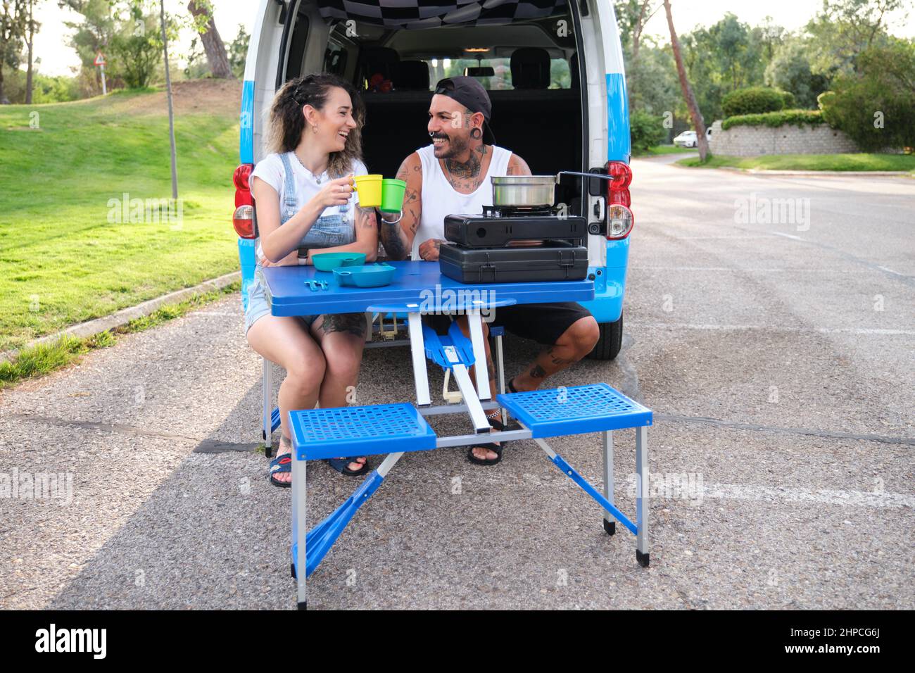 Young tattooed couple make a toast before have lunch in a picnic table ...