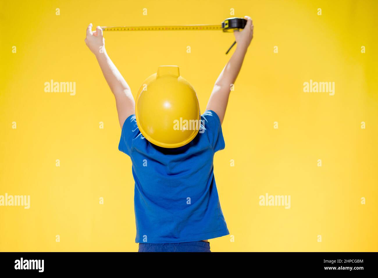 A little boy in a protective construction helmet measures with a tape ...