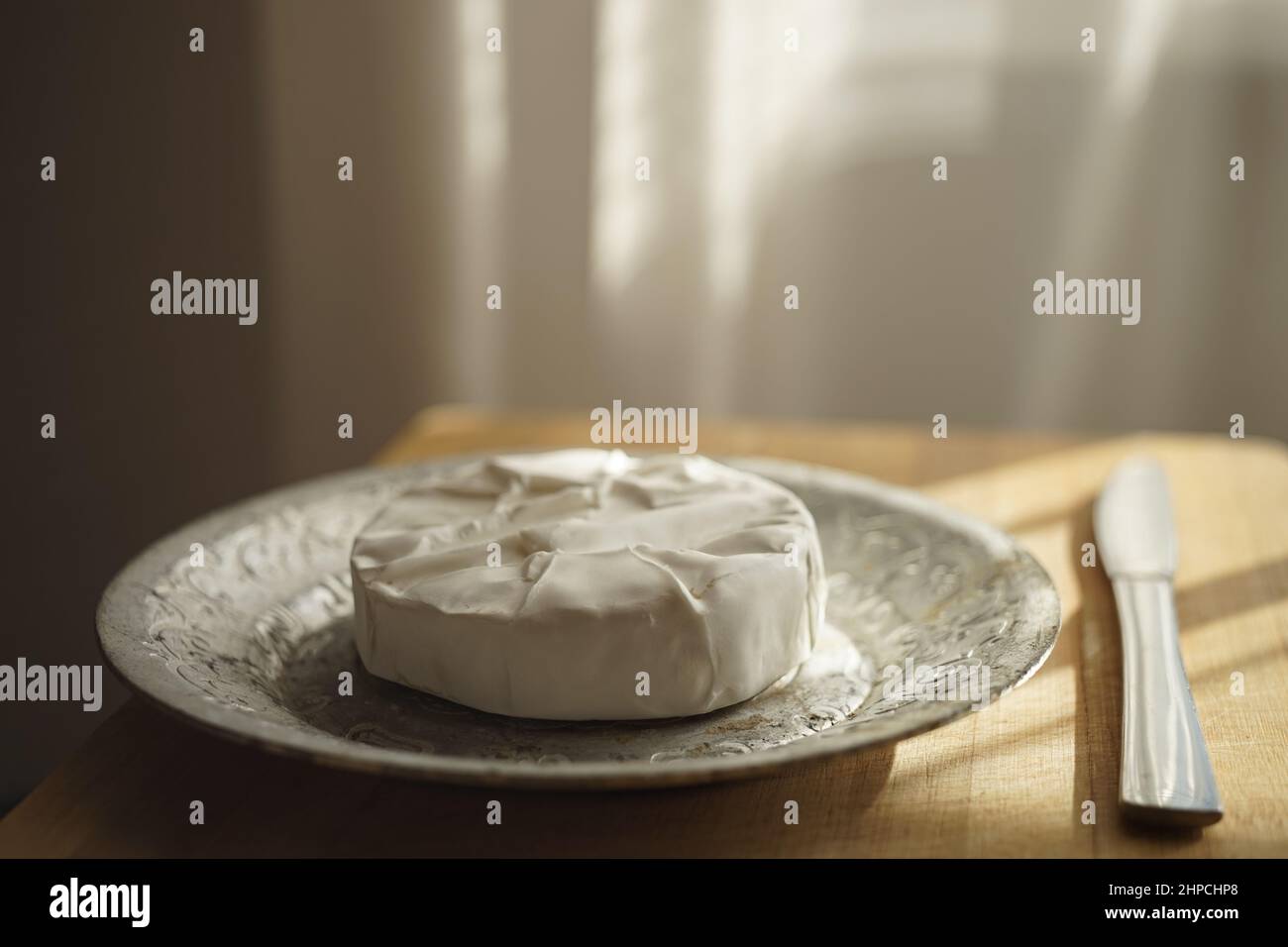 Whole round Camembert cheese on a silver plate with a knife on wooden ...