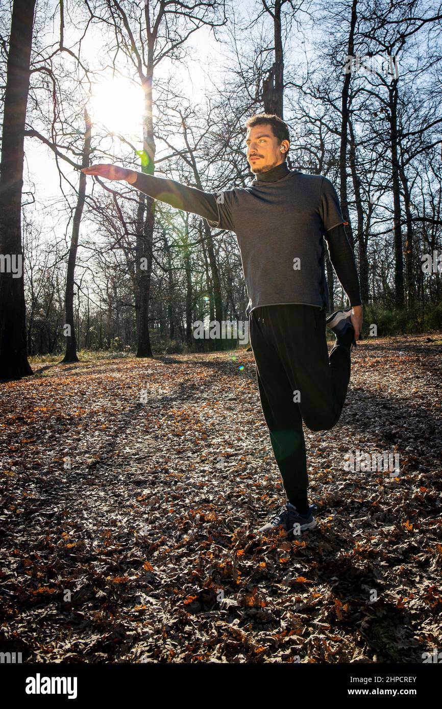 Runner is doing stretching in the woods. Young man with blue eyes and ...