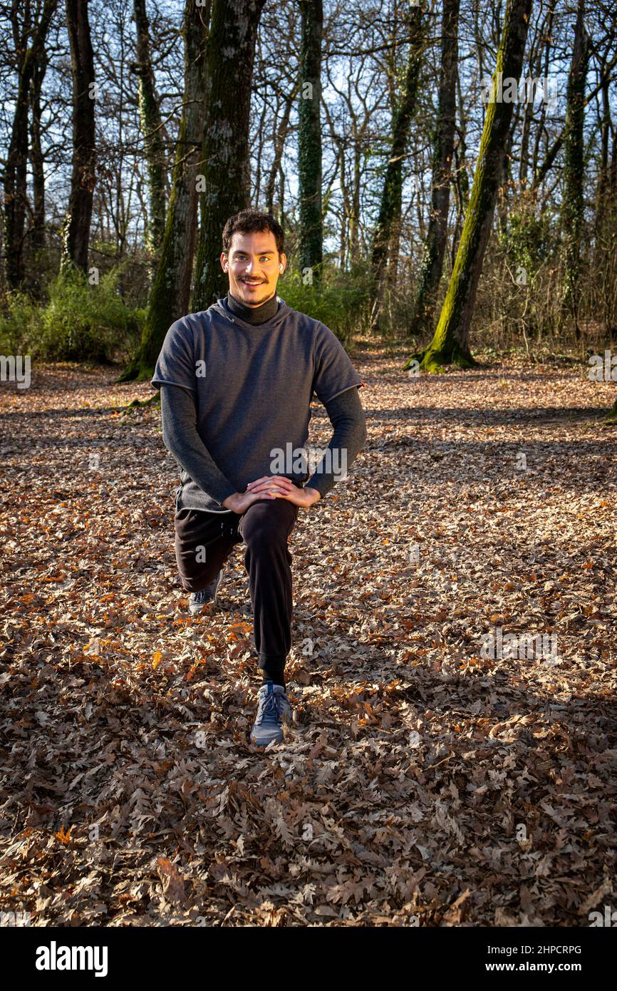 Runner is doing stretching in the woods. Young man with blue eyes and ...