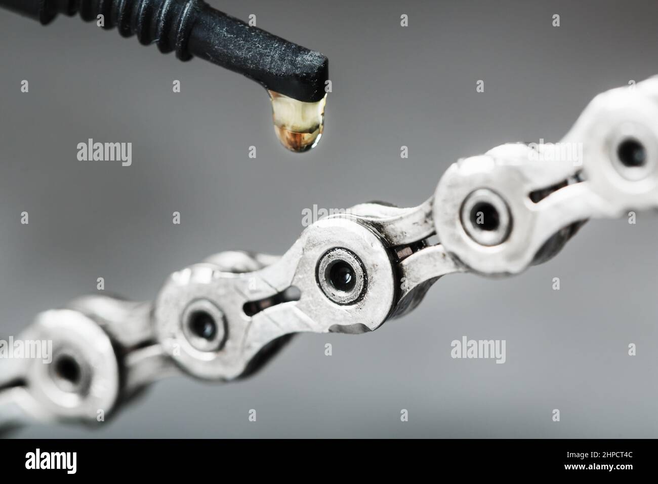 Greasing a bicycle chain with a drop of golden oil close-up on a gray ...