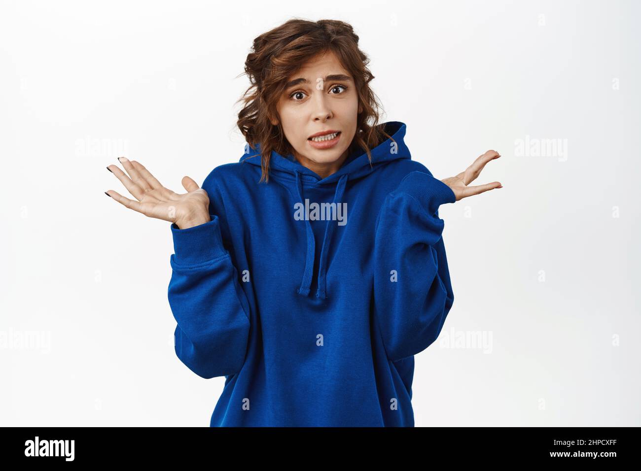 cute young woman shrugging shoulders, looking awkward and uncomfortable ...