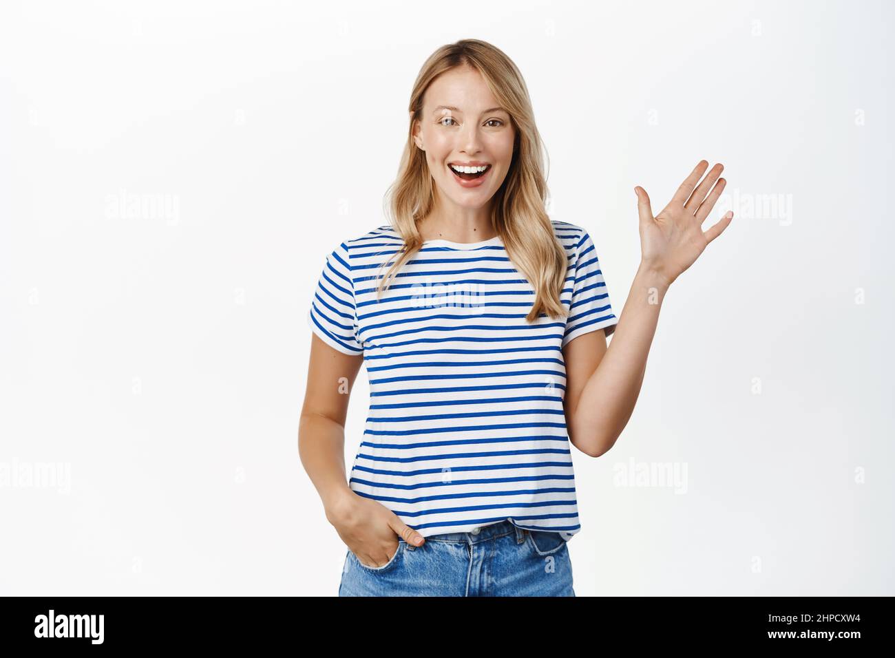 Happy and friendly blond girl smiling, waving hand and saying hello, hi ...