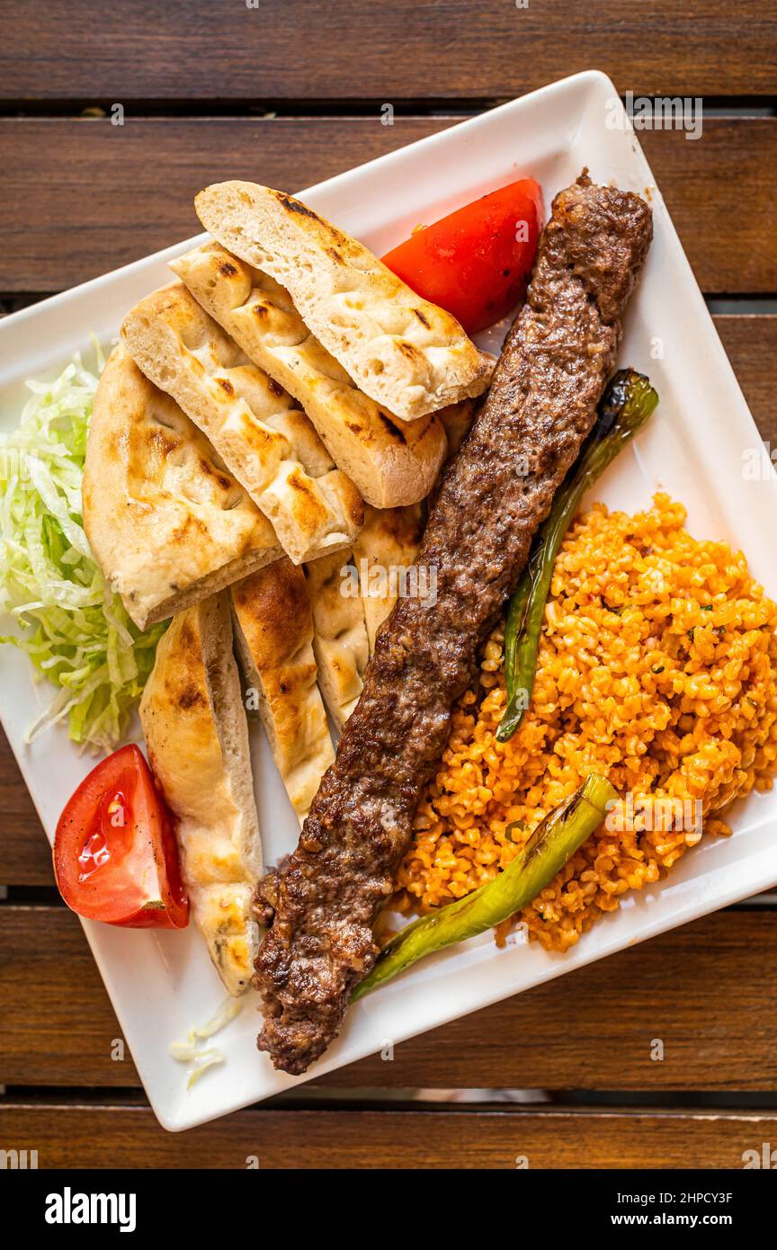 Turkish Adana kebab on a plate with marinated peppers, bread and rice ...