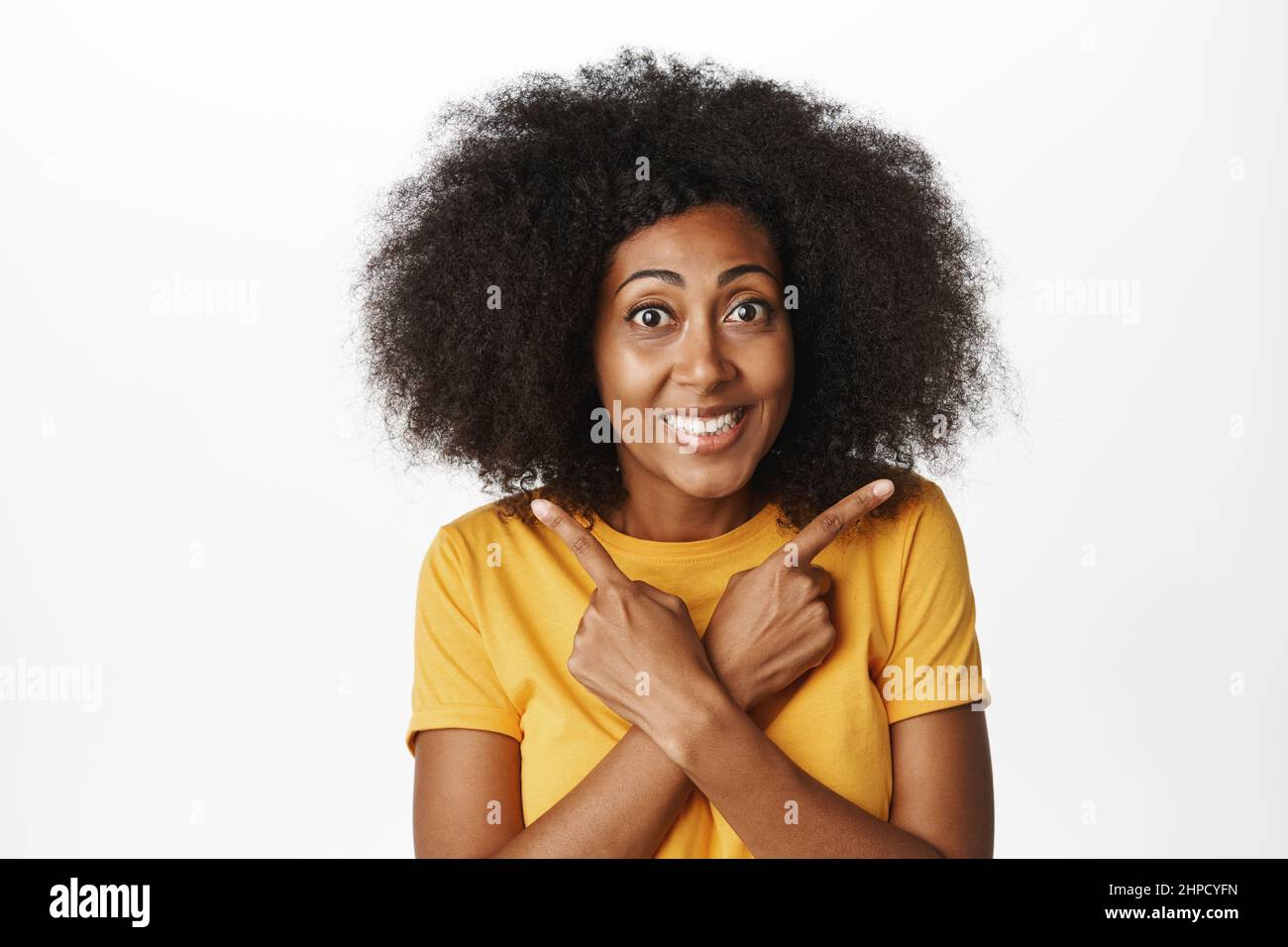 Image of indecisive african american woman points sideways and smiles ...