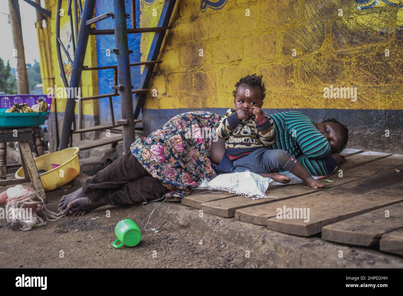 A woman takes a nap close by her daughter by the streets in Kibera ...
