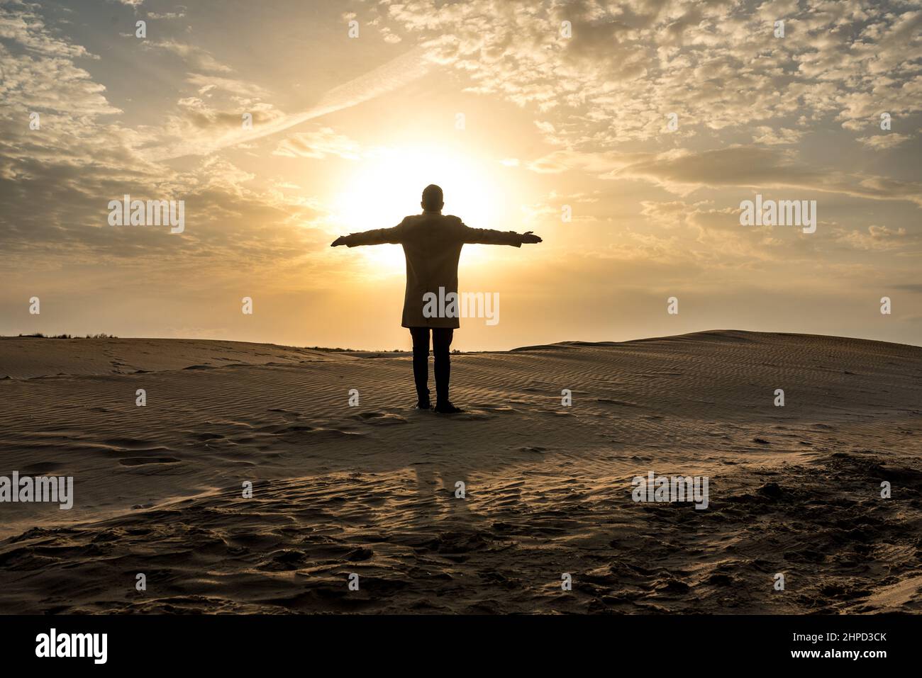 Silhouette of a man with arms outstretched on the dunes at sunset ...