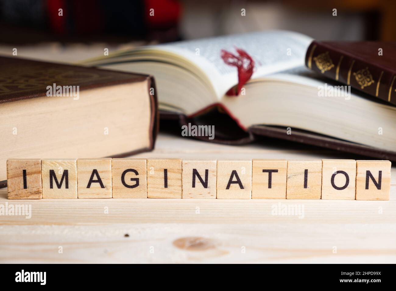Word IMAGINATION written with wooden blocks, next to books on a table ...
