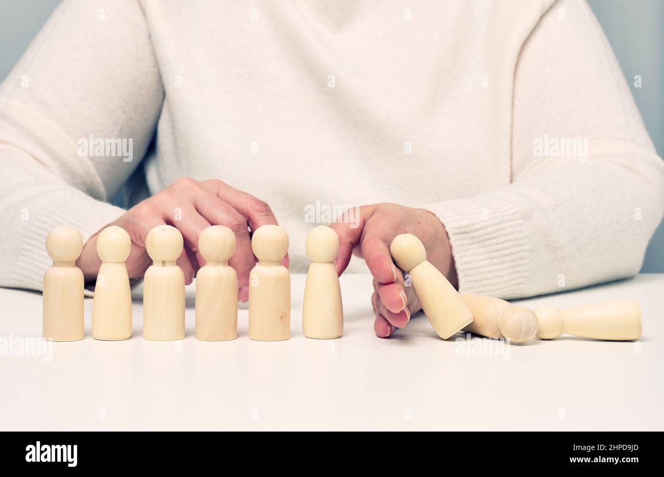 hand stops the fall of wooden figurines of men on a white background ...