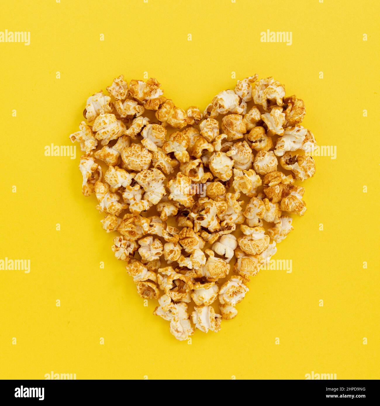 heart shaped caramel popcorn on yellow, close up with copy space for ...