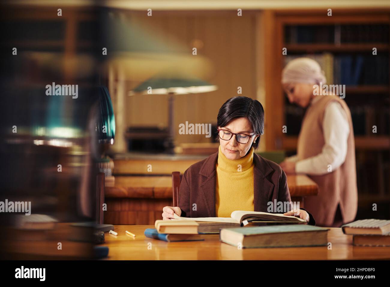 Warm toned portrait of adult female student reading book in classic ...