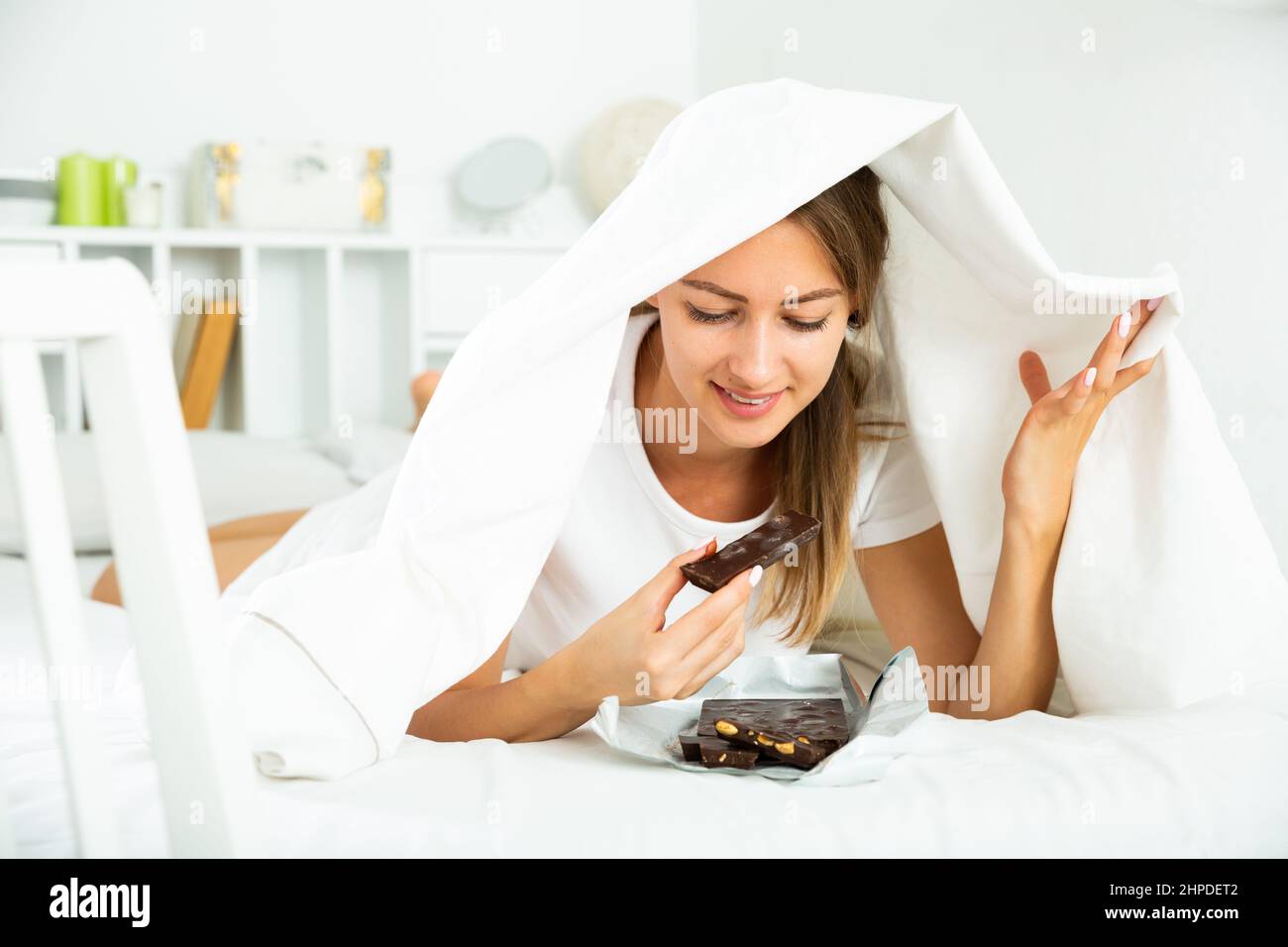Happy girl hiding under sheet with sweets indoors Stock Photo - Alamy