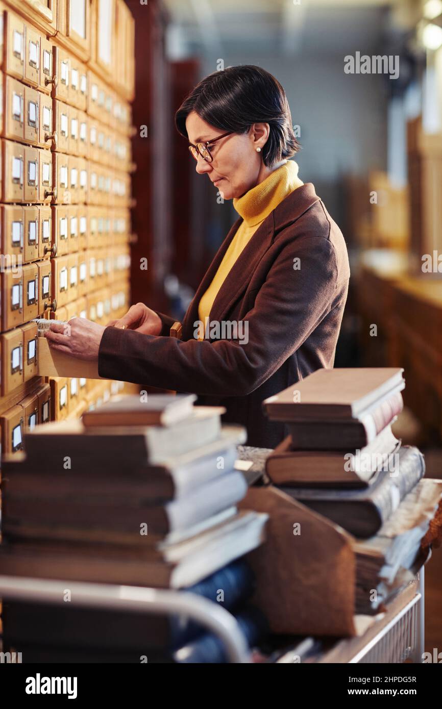 Vertical portrait of adult woman searching for book in library ...