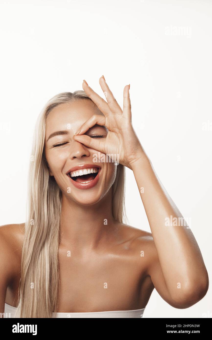 Vertical shot of happy laughing woman model with blond hair, showing ok ...