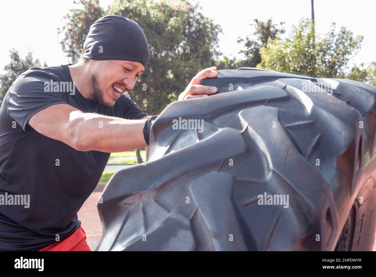 Latin man smiling while exercising lifting and pushing a big wheel in a ...