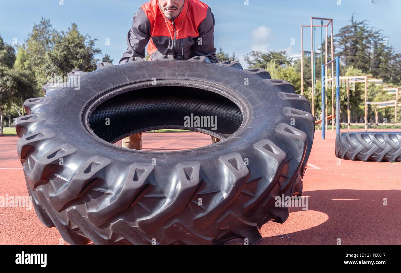 Young man lifting and pushing a huge tire working out with functional ...