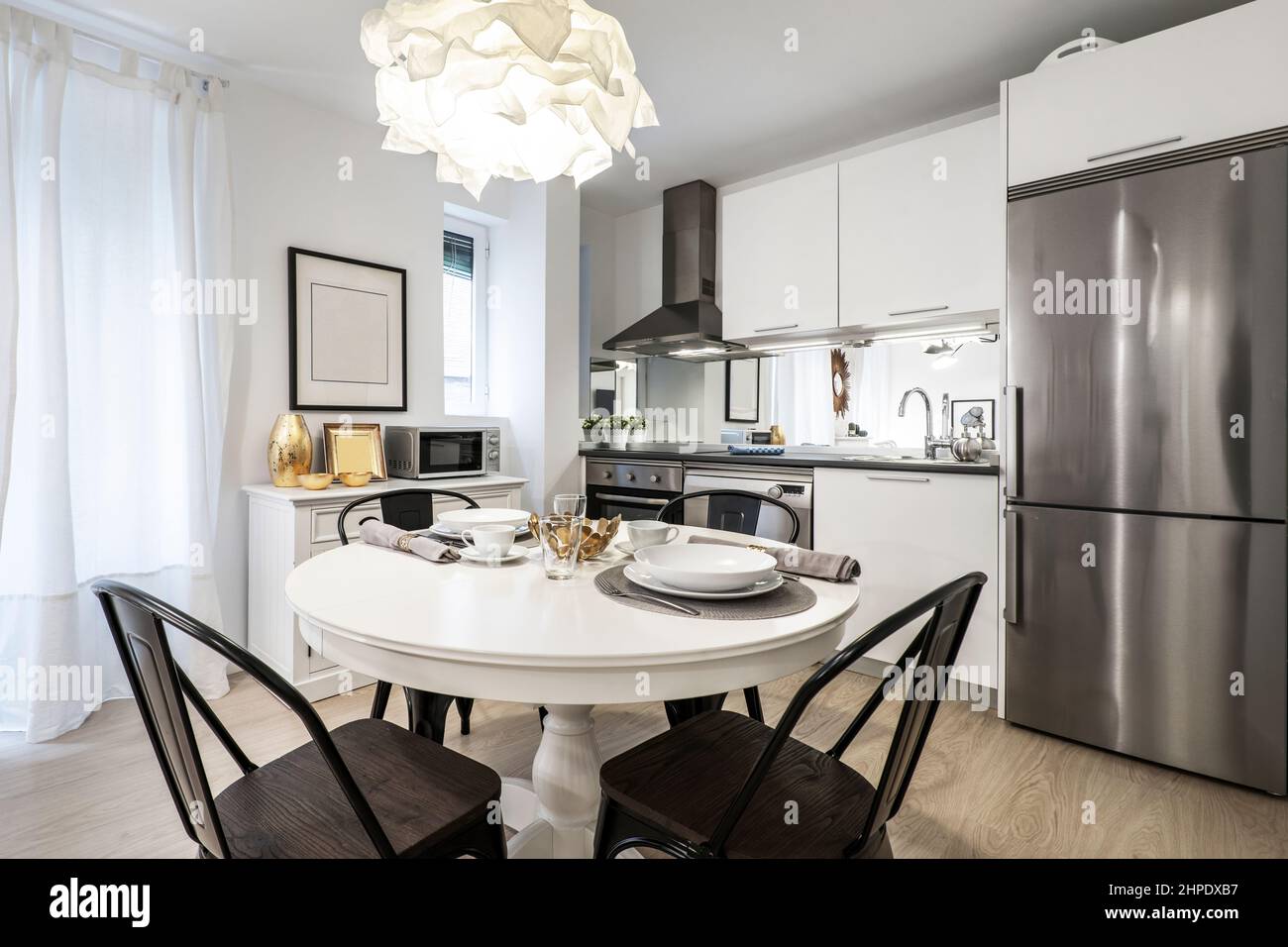 Round white dining table with food service next to kitchen of white ...