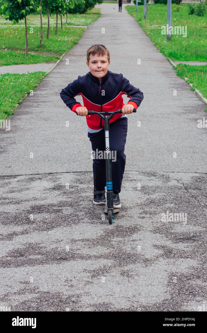 Cute boy riding scooter in a summer park. Happy teenager riding a ...