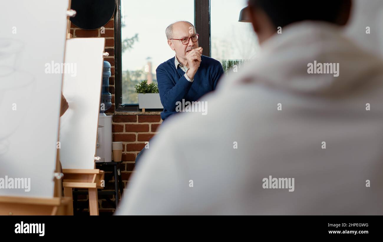 Senior man teaching art students to draw artwork on canvas, attending ...