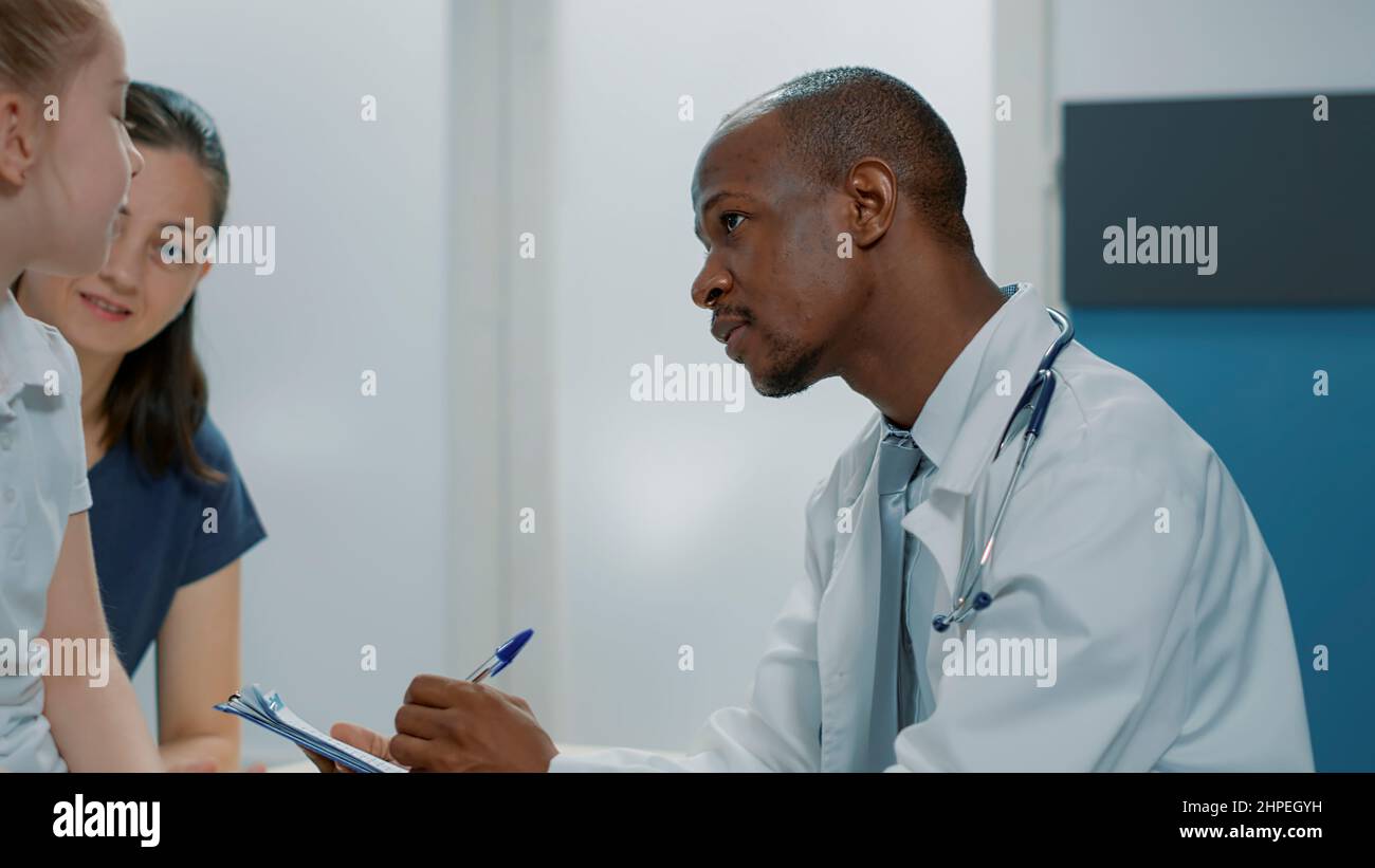 Pediatrician holding clipboard documents and taking notes in cabinet at ...