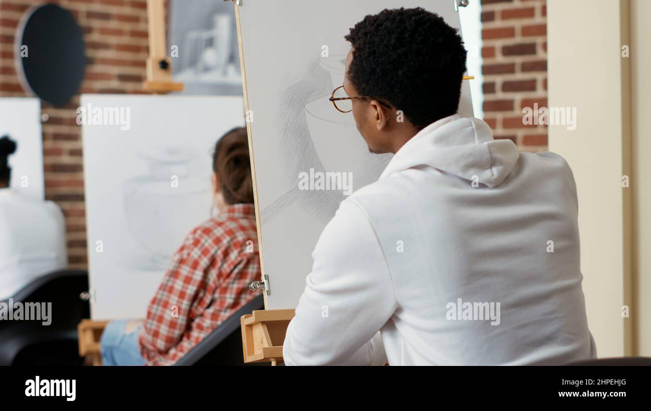 Young student looking at vase model to draw sketch on canvas, attending ...
