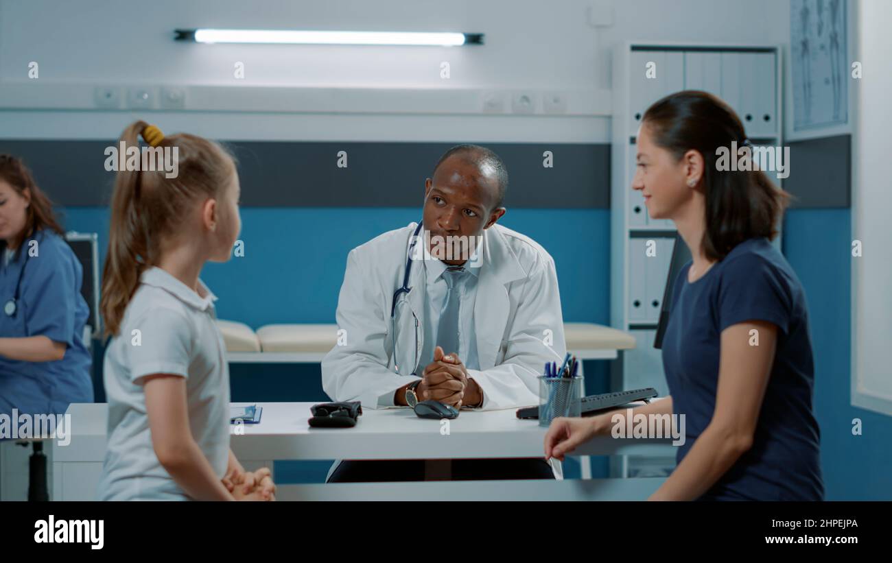 General practitioner greeting mother and child in cabinet, attending ...
