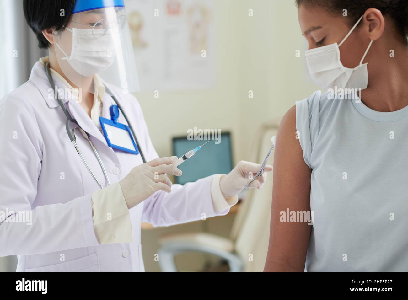 Asian doctor in protective wear making injection to teenage girl in her ...