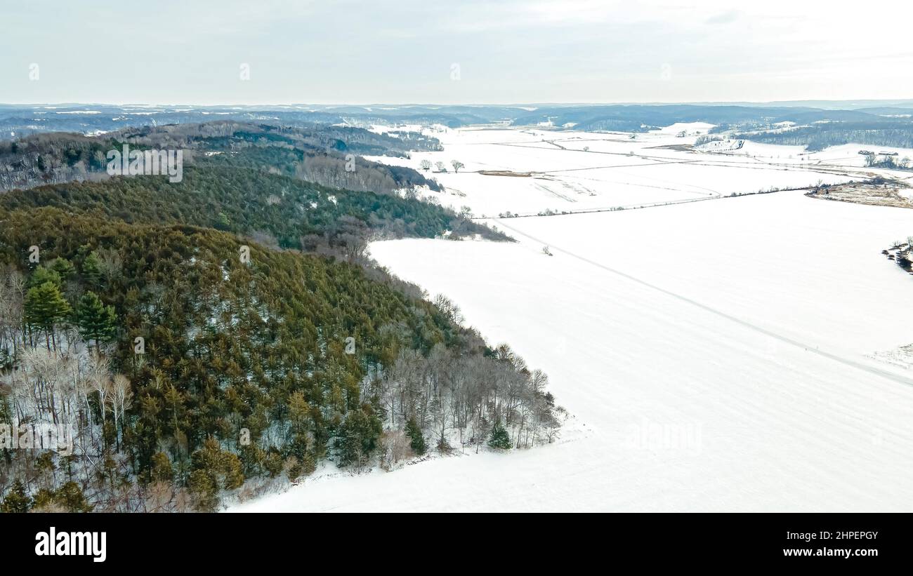 Snow covers the hills and fields with farm fields between the slopes ...