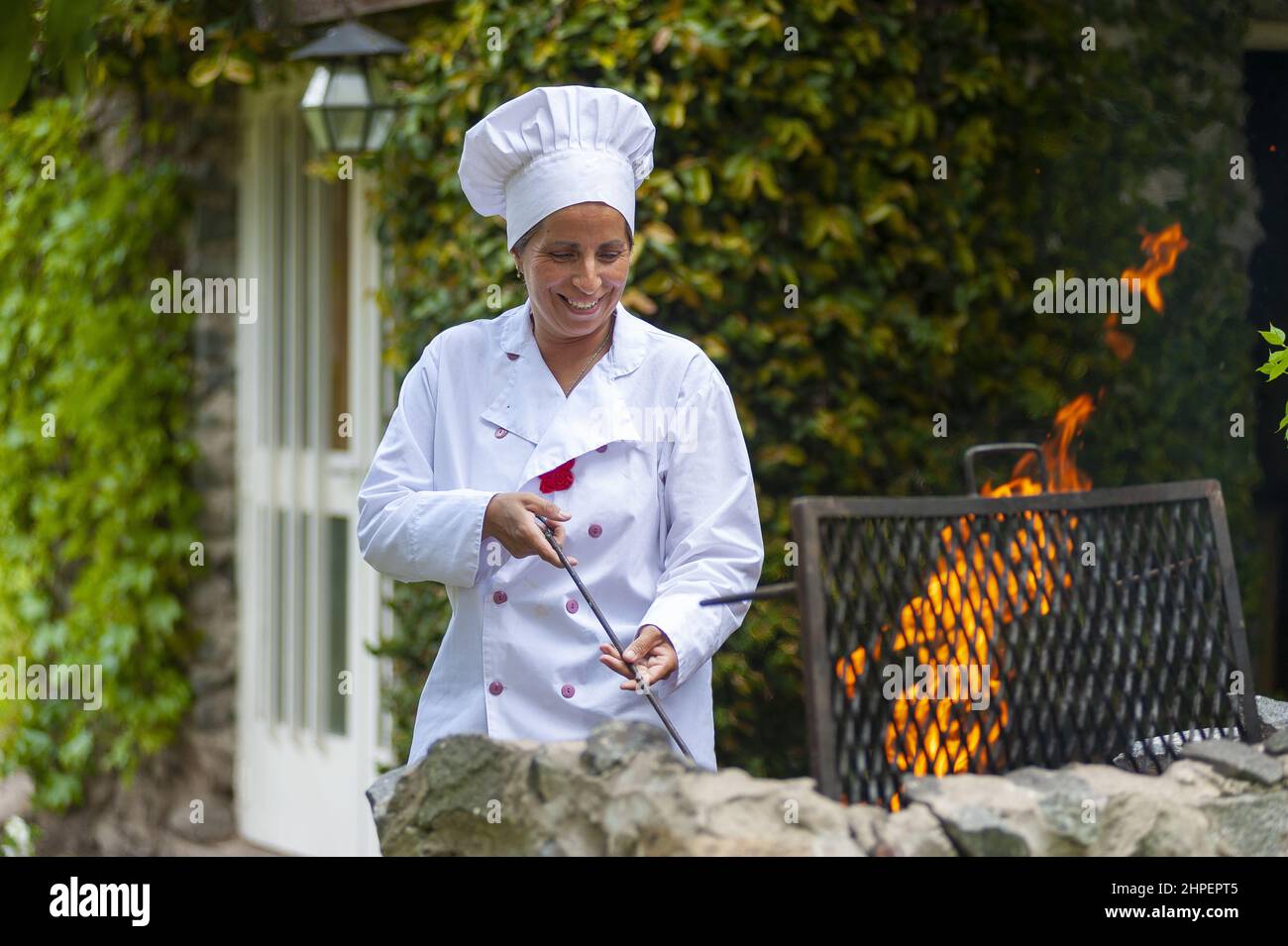 Hispanic female chef in a white uniform grilling meat on fire on an ...