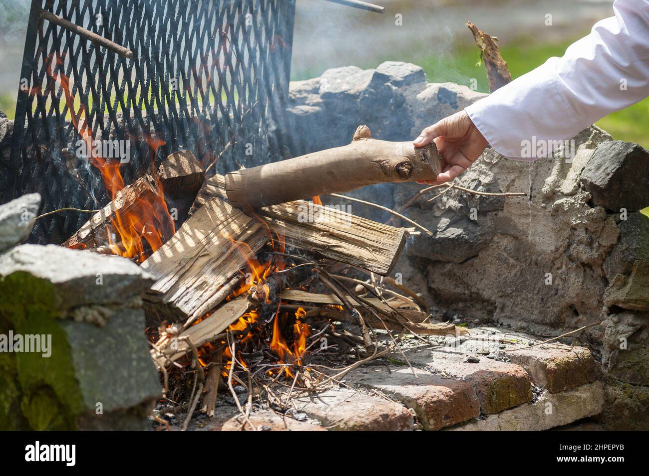 Closeup of a female hand adding a piece of wood on fire for a grill ...