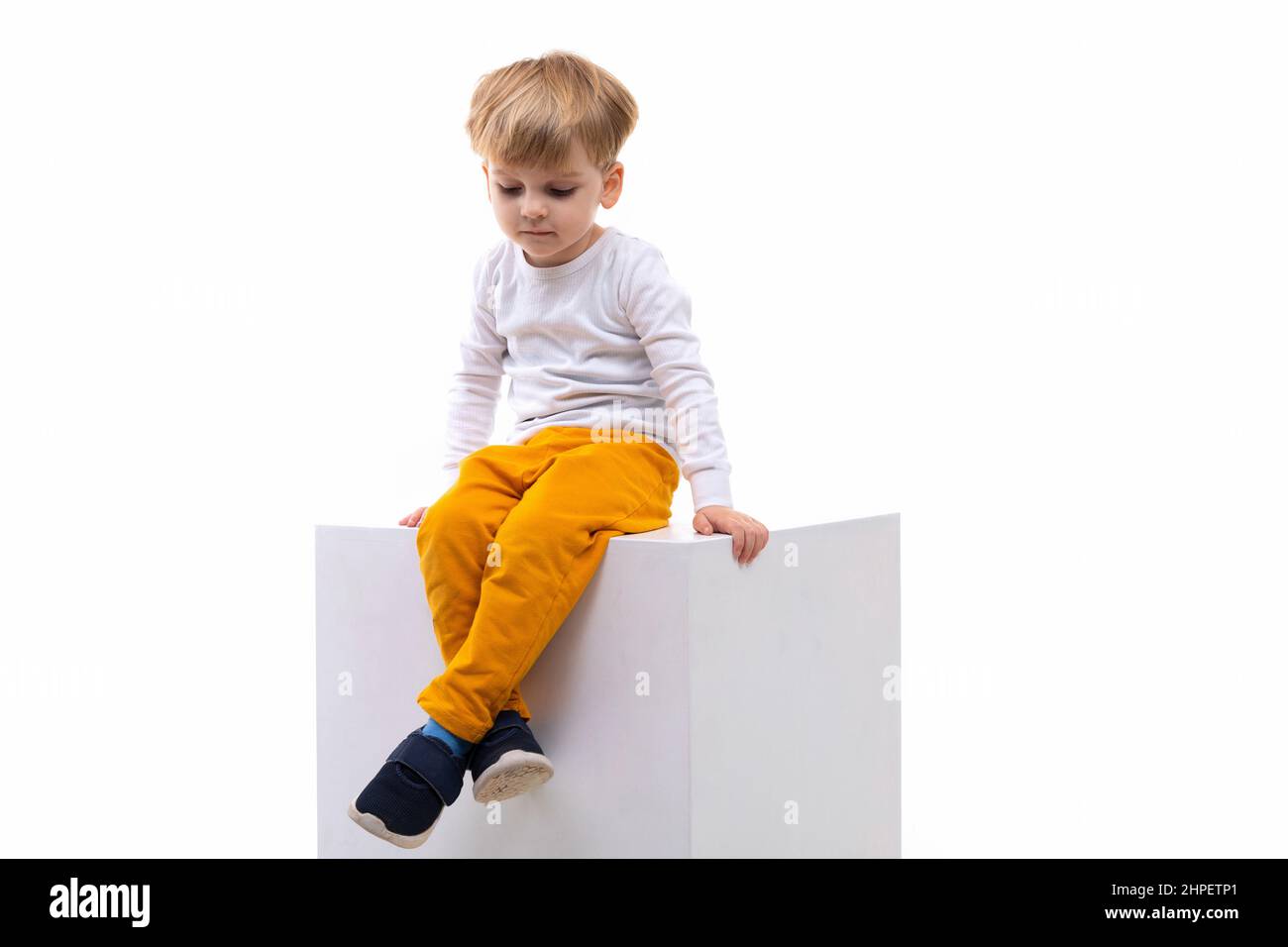 little blond child is bored sitting on a white background Stock Photo ...