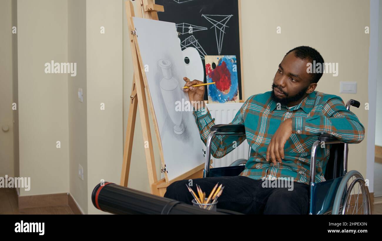 African american man with disability using pencil to draw on canvas ...