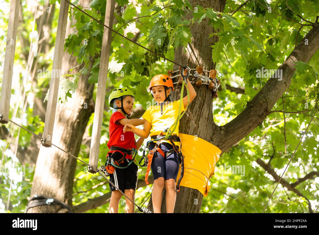 Child in forest adventure park. Kids climb on high rope trail. Agility ...