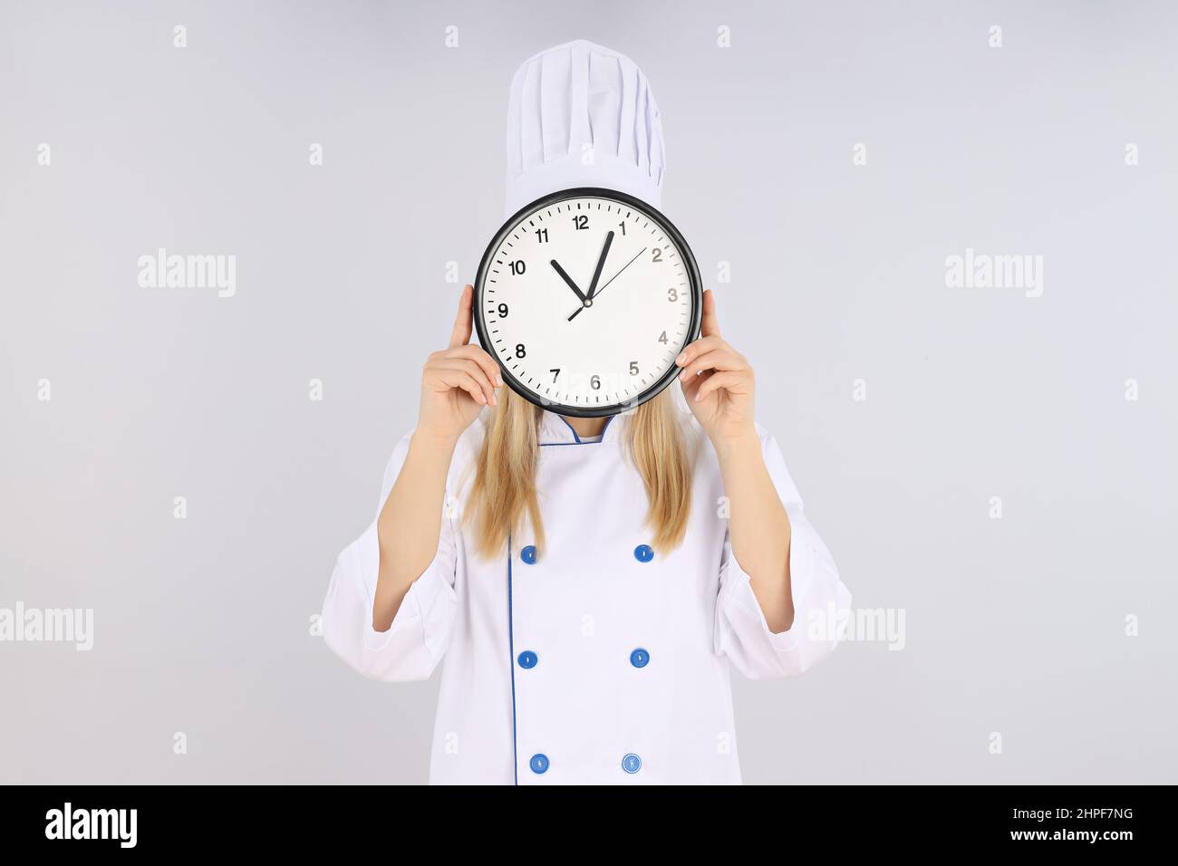 Female chef with clock on light background Stock Photo - Alamy