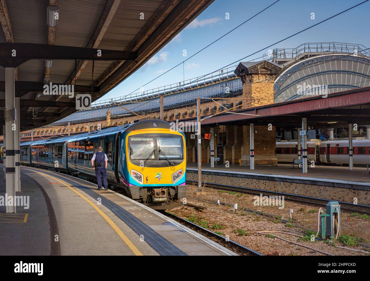 A train alongside a railway station platform. Stanchions support a ...