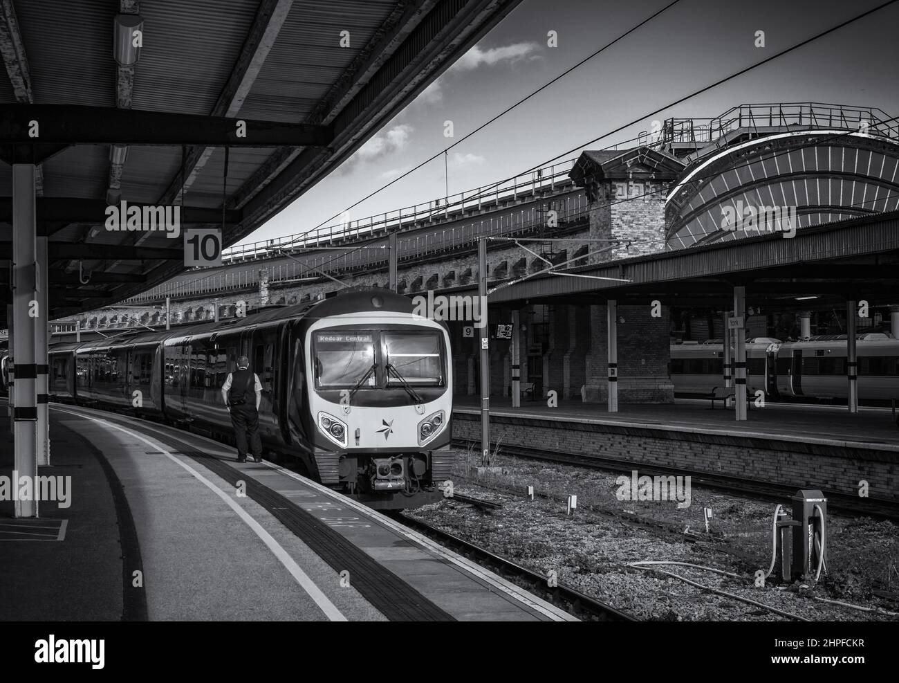 A train alongside a railway station platform. Stanchions support a ...