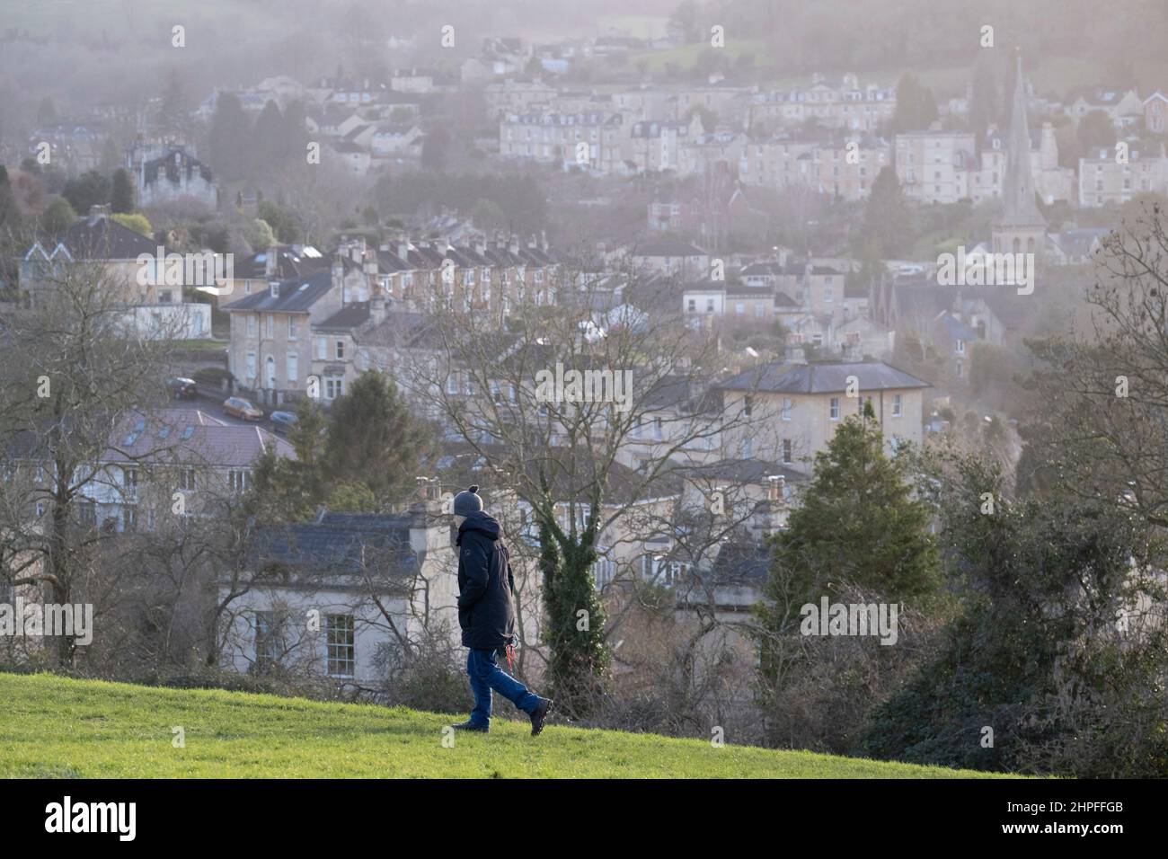 With homes and other properties beyond her, a walker climbs a hill ...