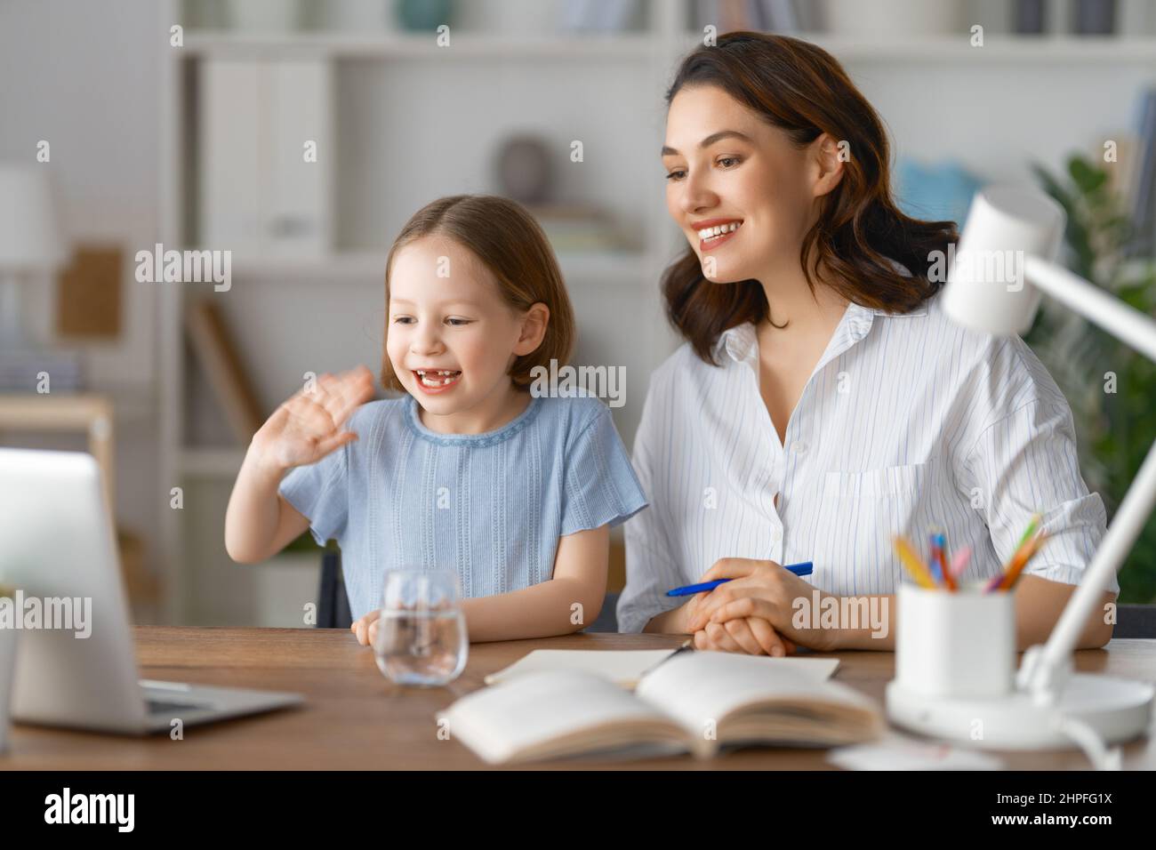 Happy child and adult are sitting at desk. Girl doing homework or ...