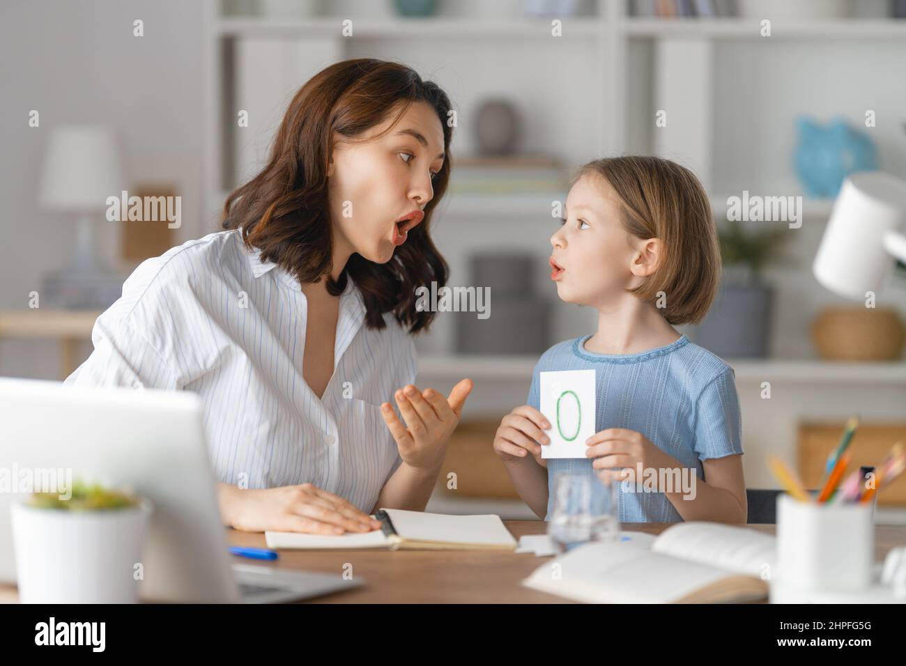 Happy child and adult are sitting at desk. Girl doing homework or ...
