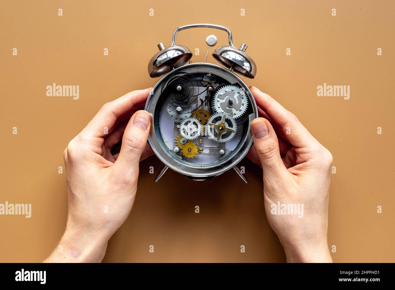 Hands holding alarm clock mechanism with steel gears and wheels close ...
